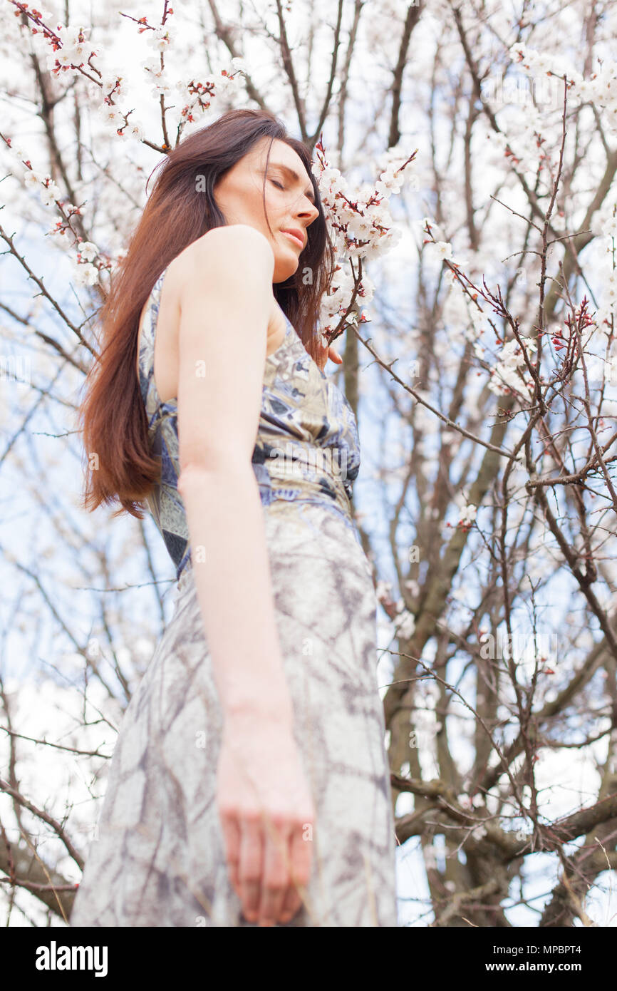 slender brown-haired woman with blue eyes in a blooming garden in full ...
