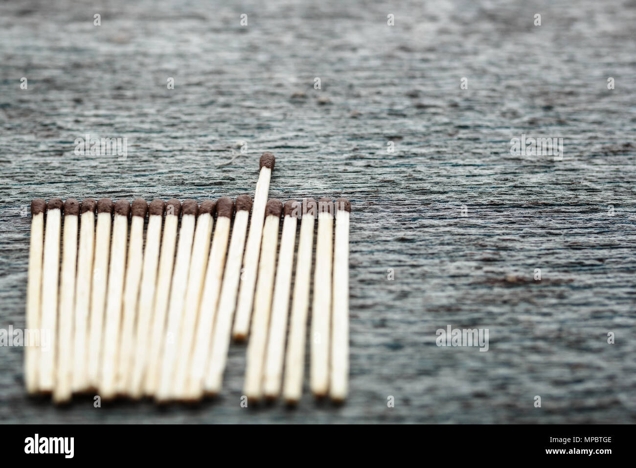 row of matches on a gray wooden background. One match stands out ...