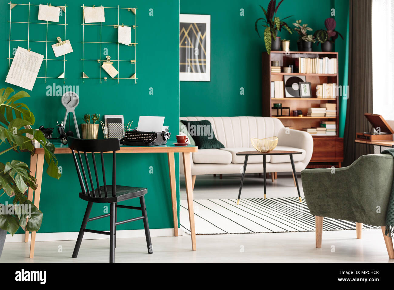 Black chair at wooden desk in green open space interior with armchair ...