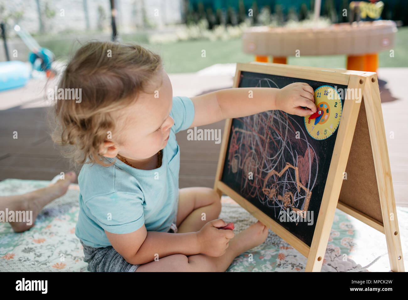 A toddler drawing on a chalkboard and learning to tell time. A portrait ...