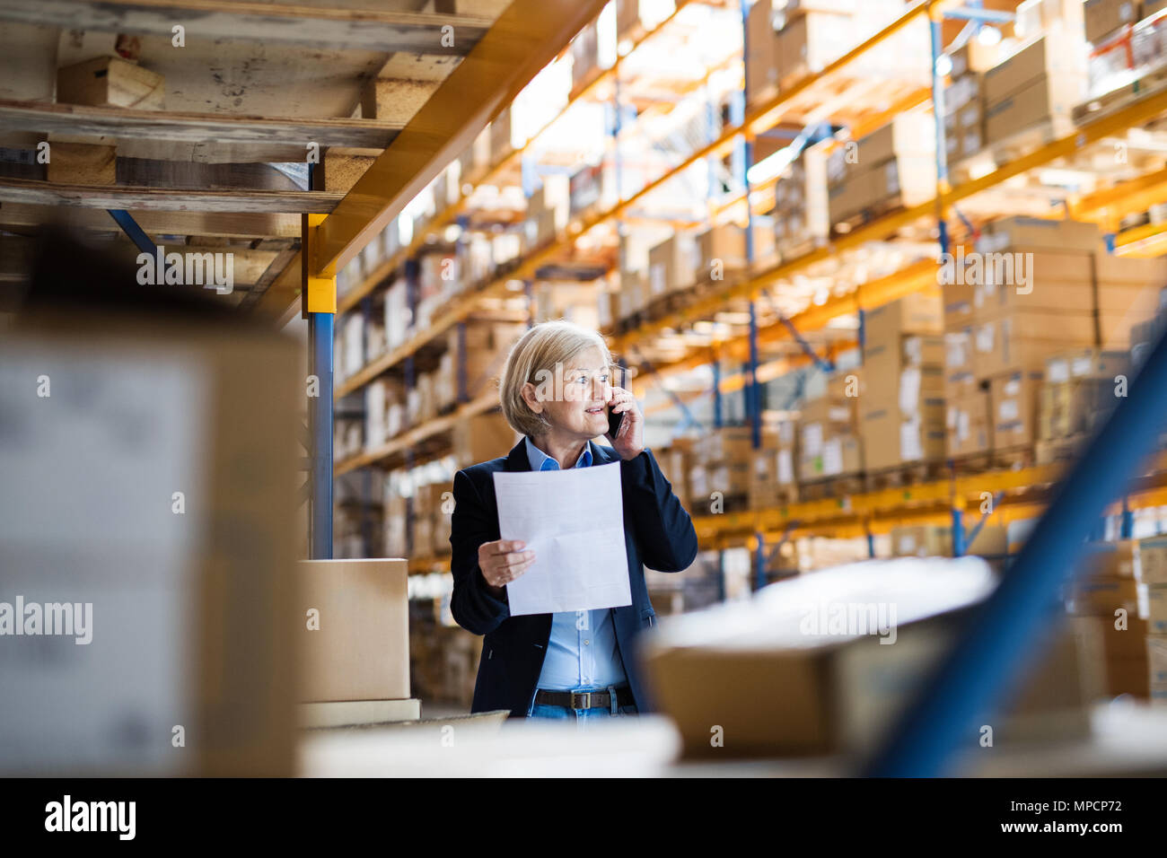 Senior woman warehouse manager or supervisor with smartphone making a ...