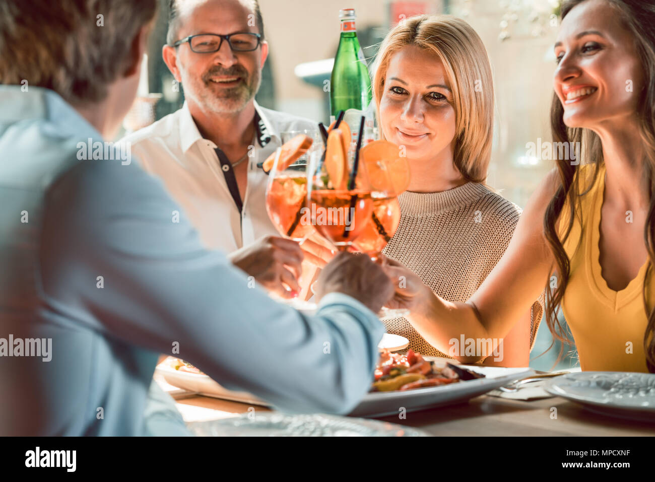 Young friends toasting with cocktails before eating seafood at a ...