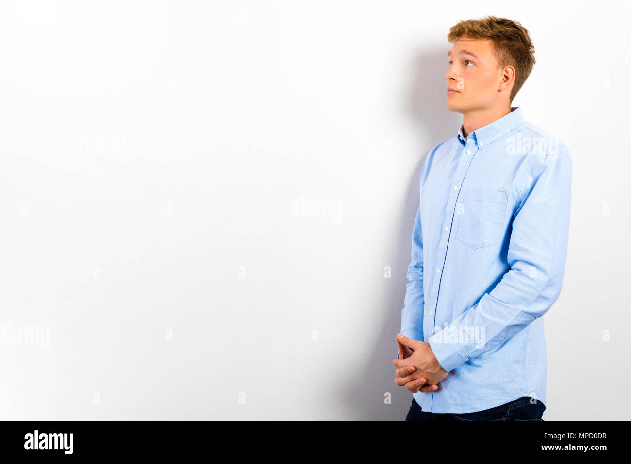 Young man standing against wall looking on side smiling Stock Photo - Alamy