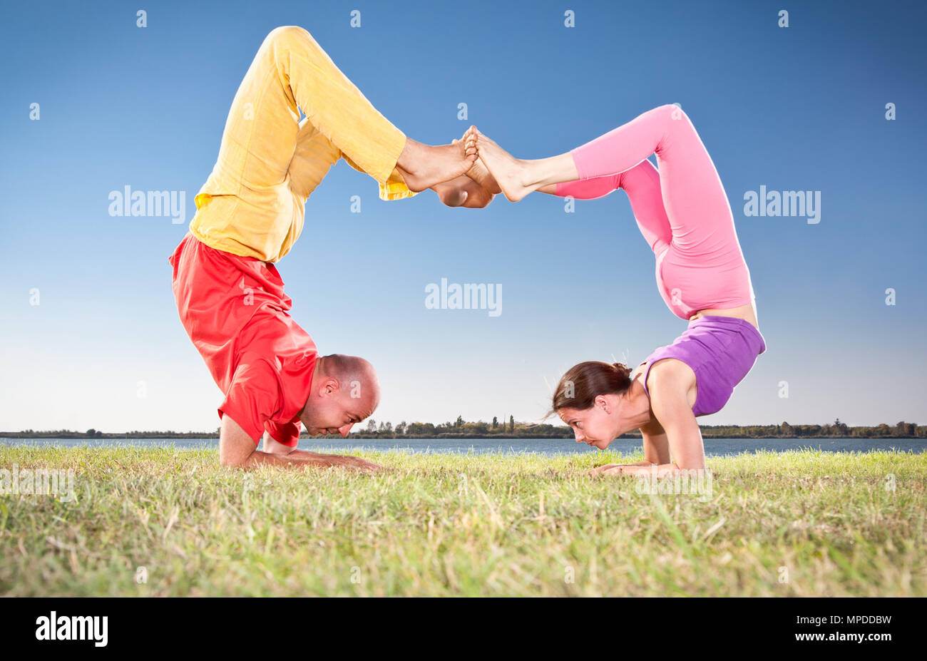 Yoga couple, man and woman doing Vrschikasana scorpion pose on lake ...