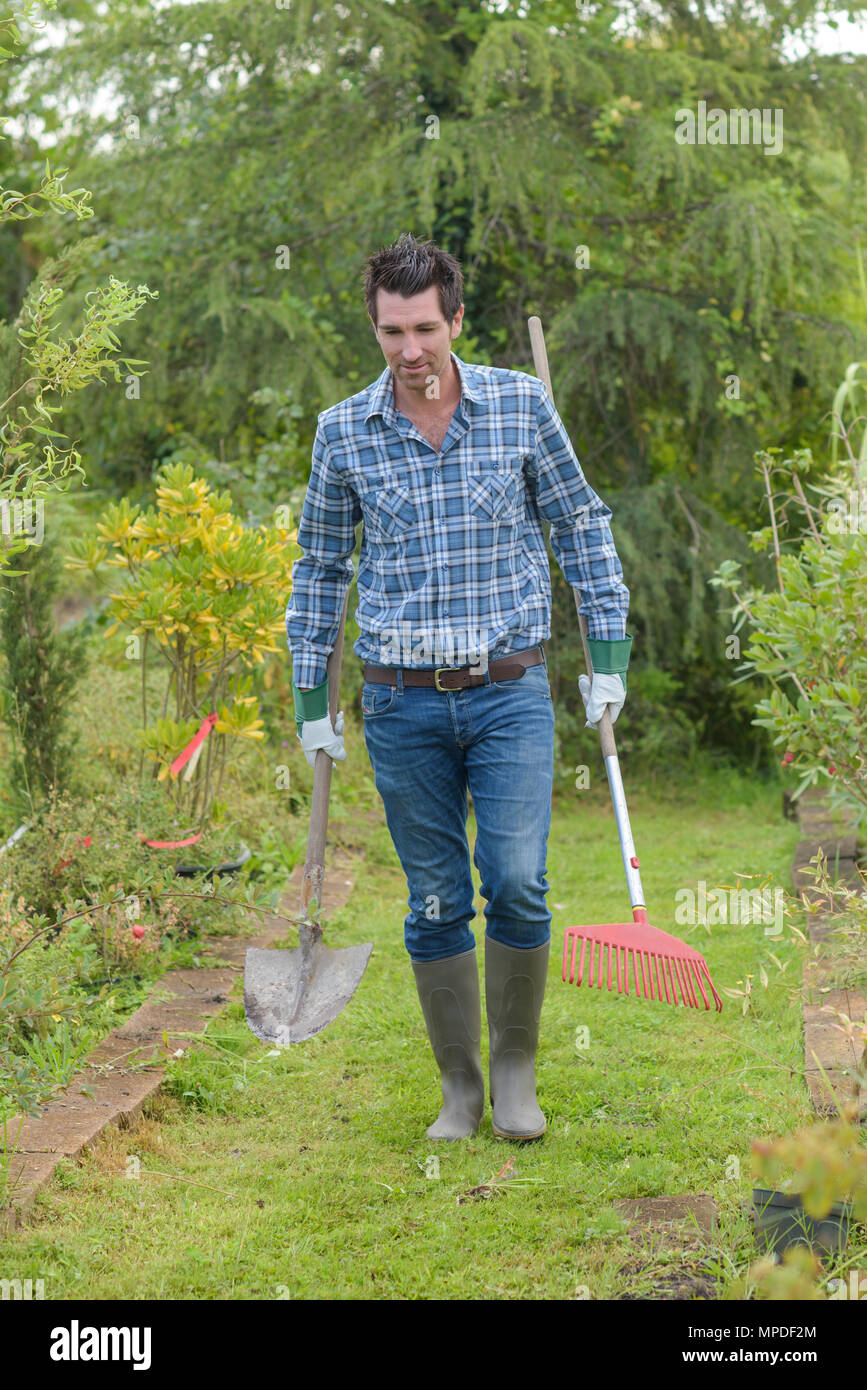 Gardener carrying spade and rake Stock Photo - Alamy