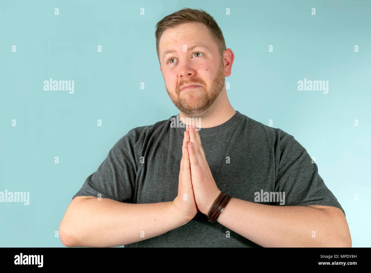 Half body portrait of young man with hands together in prayer looking ...