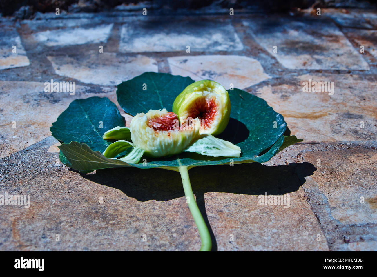 Split ripe figs on top a large leaf atop a stone table. High angle view ...