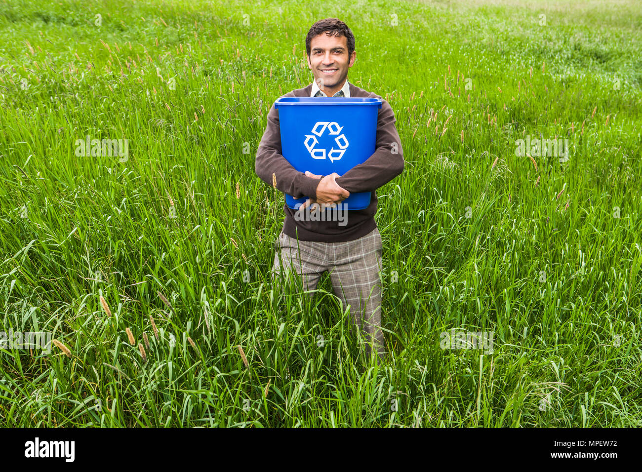 A man standing in a field of green grass and trees holding a recycle ...