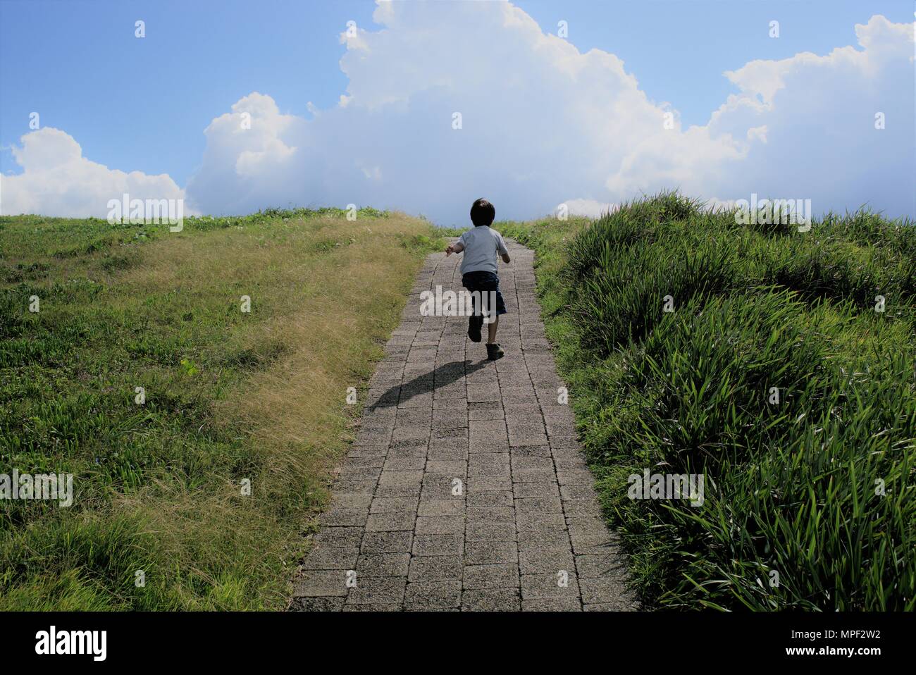 Kid running up the path on hill going towards clouds in sky ...