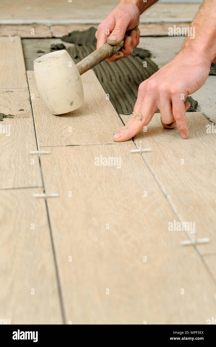 Worker installs tiles on the floor. He knocks a rubber mallet Stock ...