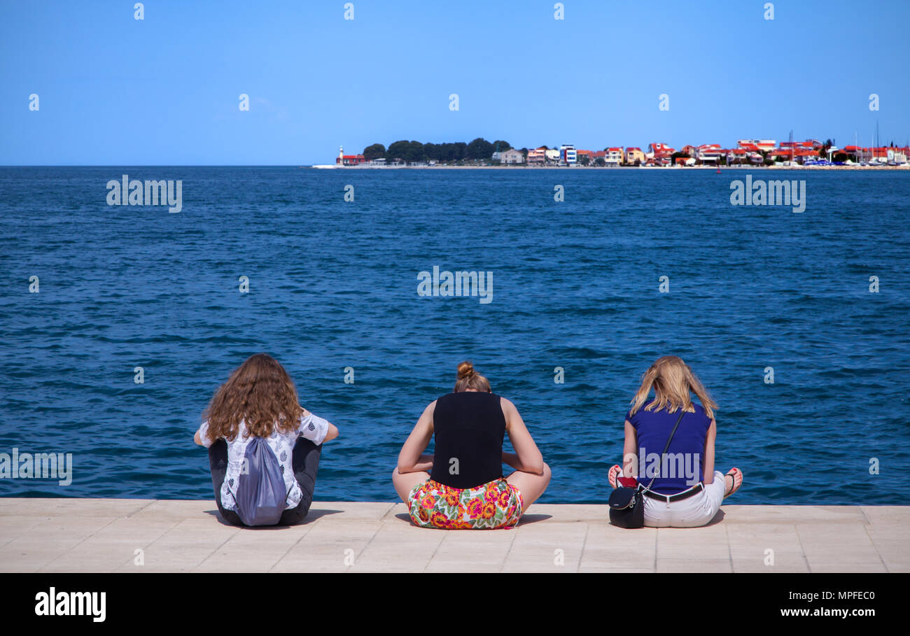 Three young women girls sitting by the sea on the seafront at the ...