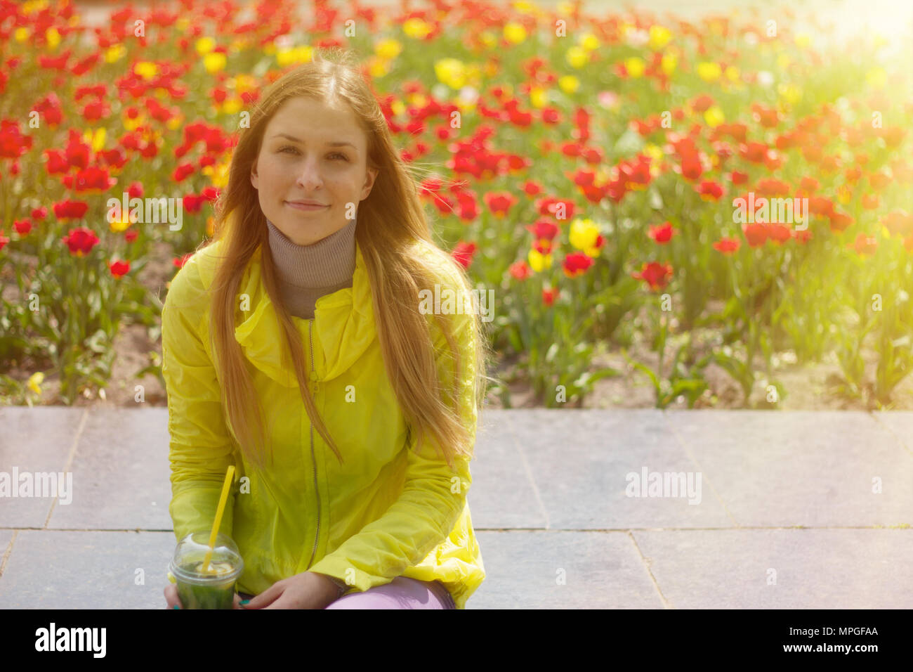 blond girl sitting next to a flower bed Stock Photo - Alamy