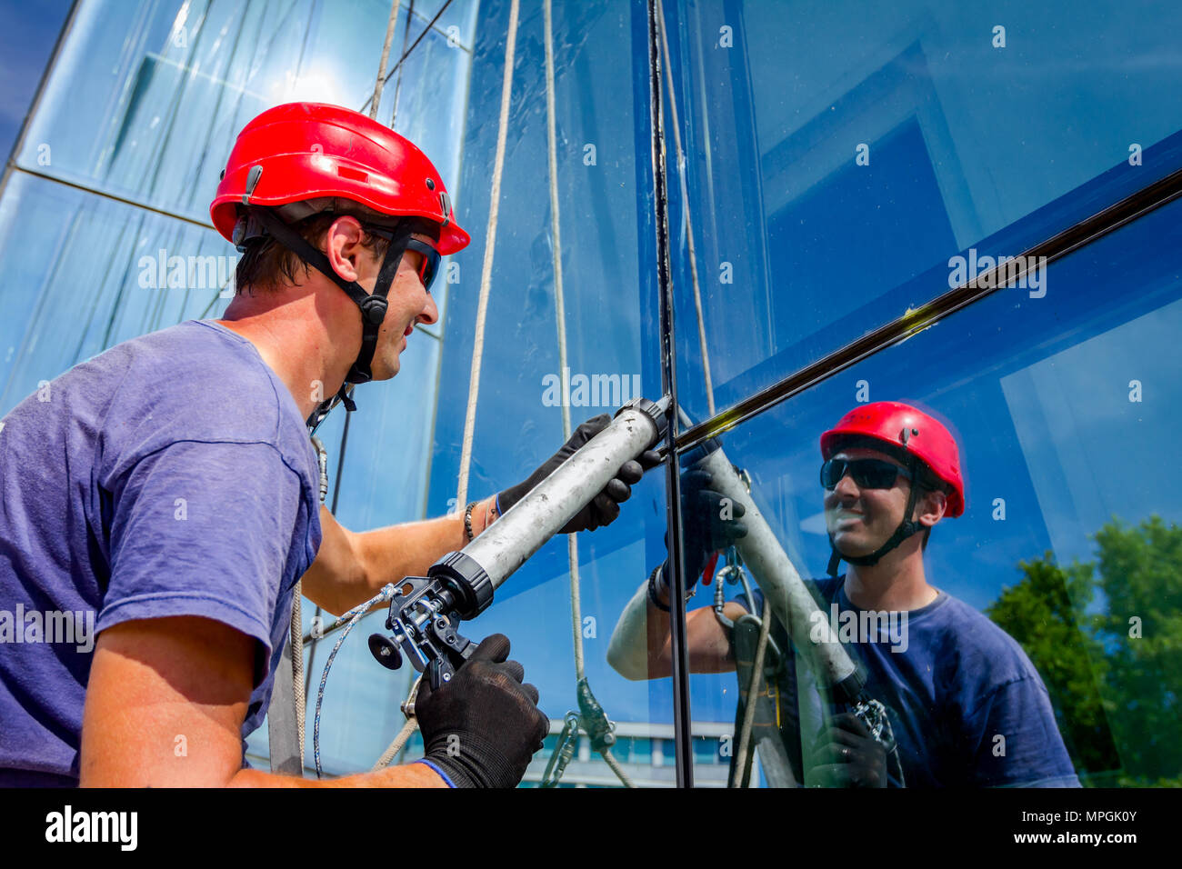 Industrial climber is applying silicone to rubber juncture among ...