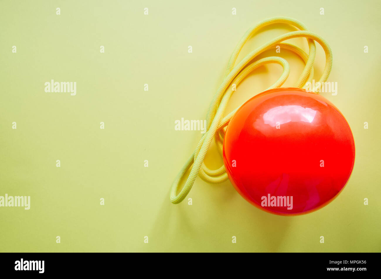 Red gymnastic ball and skipping rope on a yellow background. Sport ...