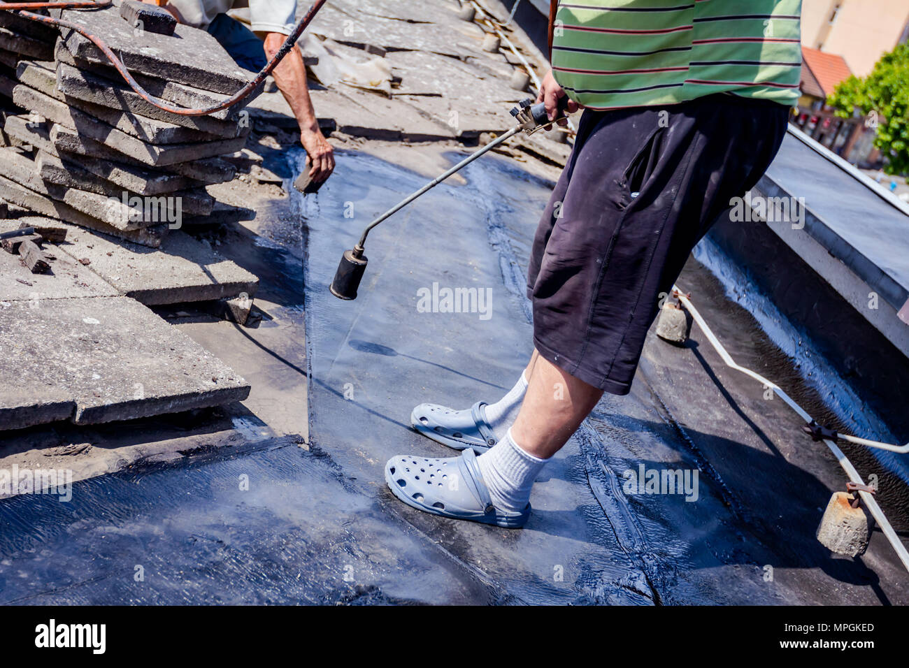 Heating and melting of bitumen surface by flame from gas torch. Worker ...