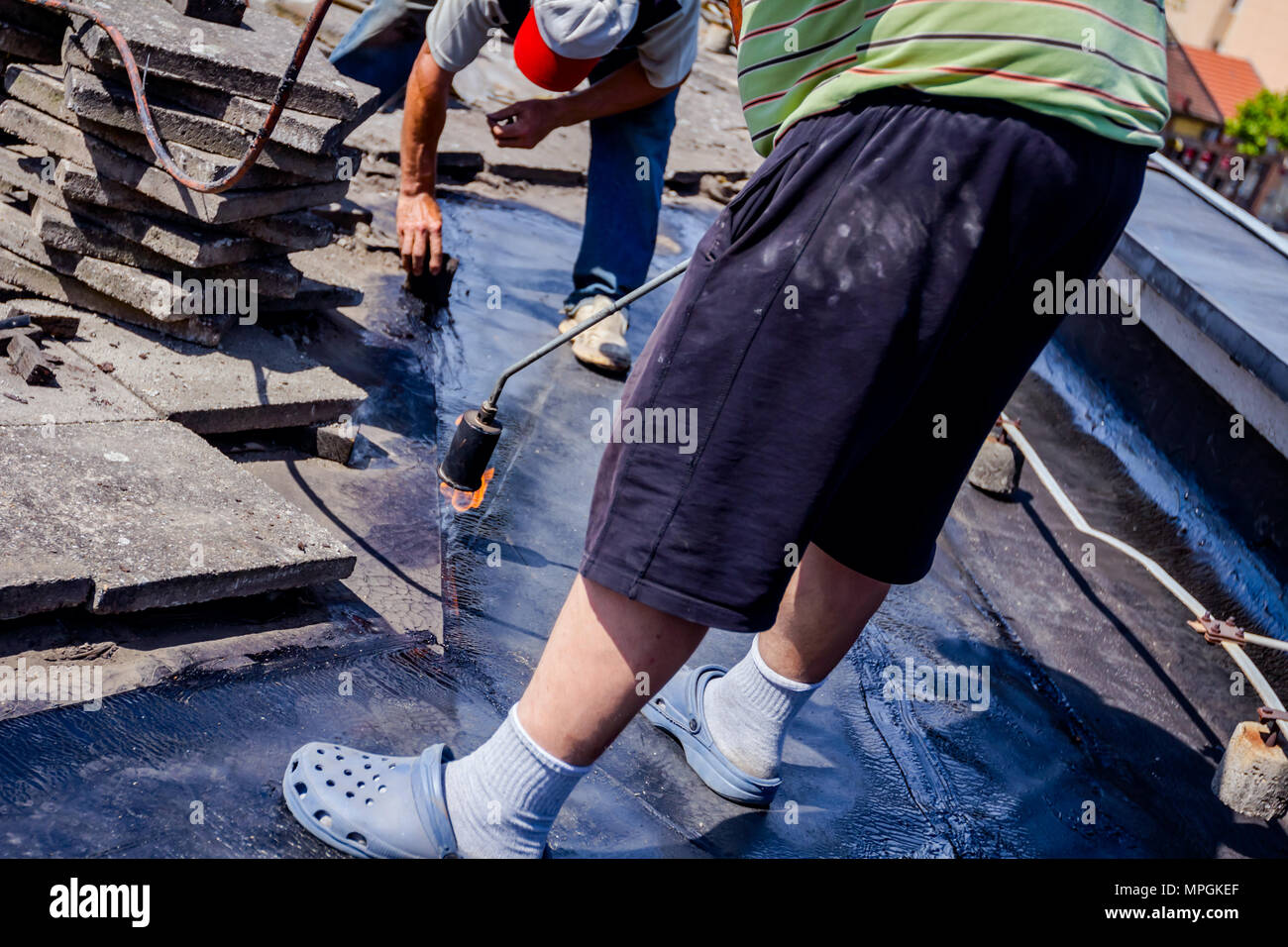 Heating and melting of bitumen surface by flame from gas torch. Worker ...