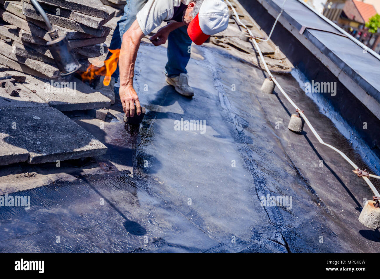 Heating and melting of bitumen surface by flame from gas torch. Worker ...