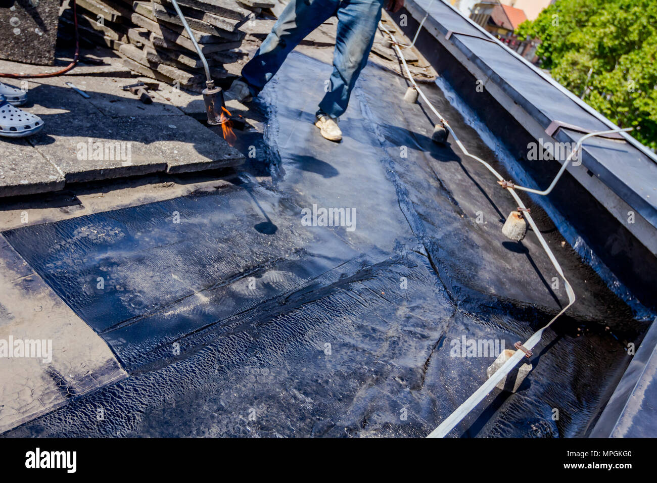 Heating and melting of bitumen surface by flame from gas torch. Worker ...