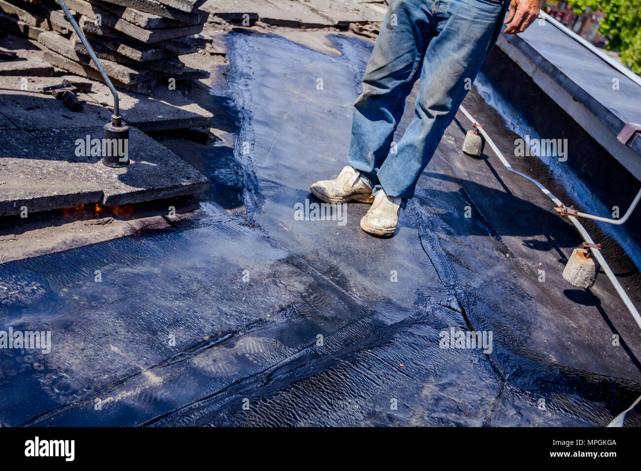 Heating and melting of bitumen surface by flame from gas torch. Worker ...