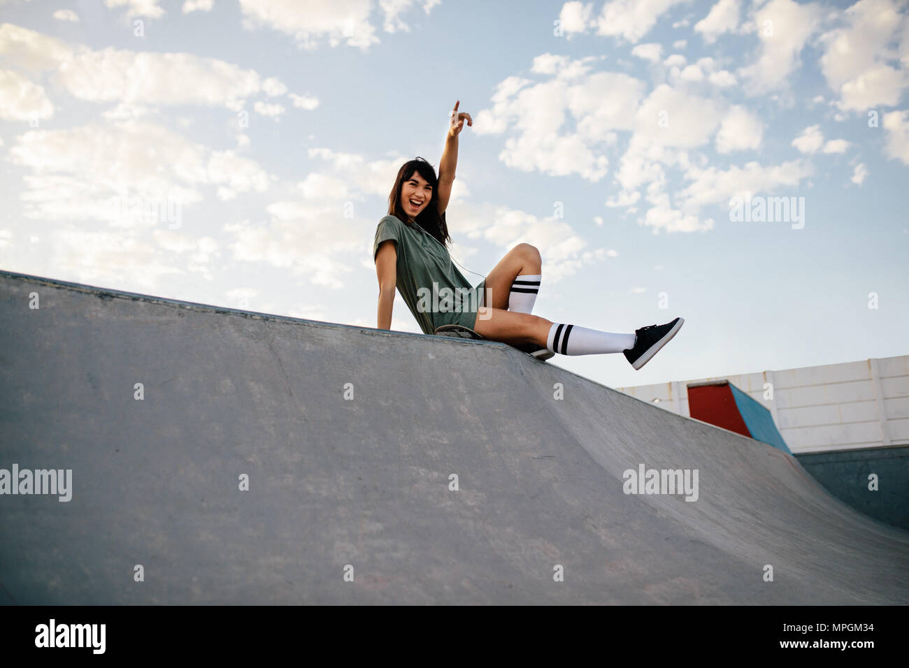 Skateboarder sitting on a ramp in skate park. Woman enjoying a day at ...