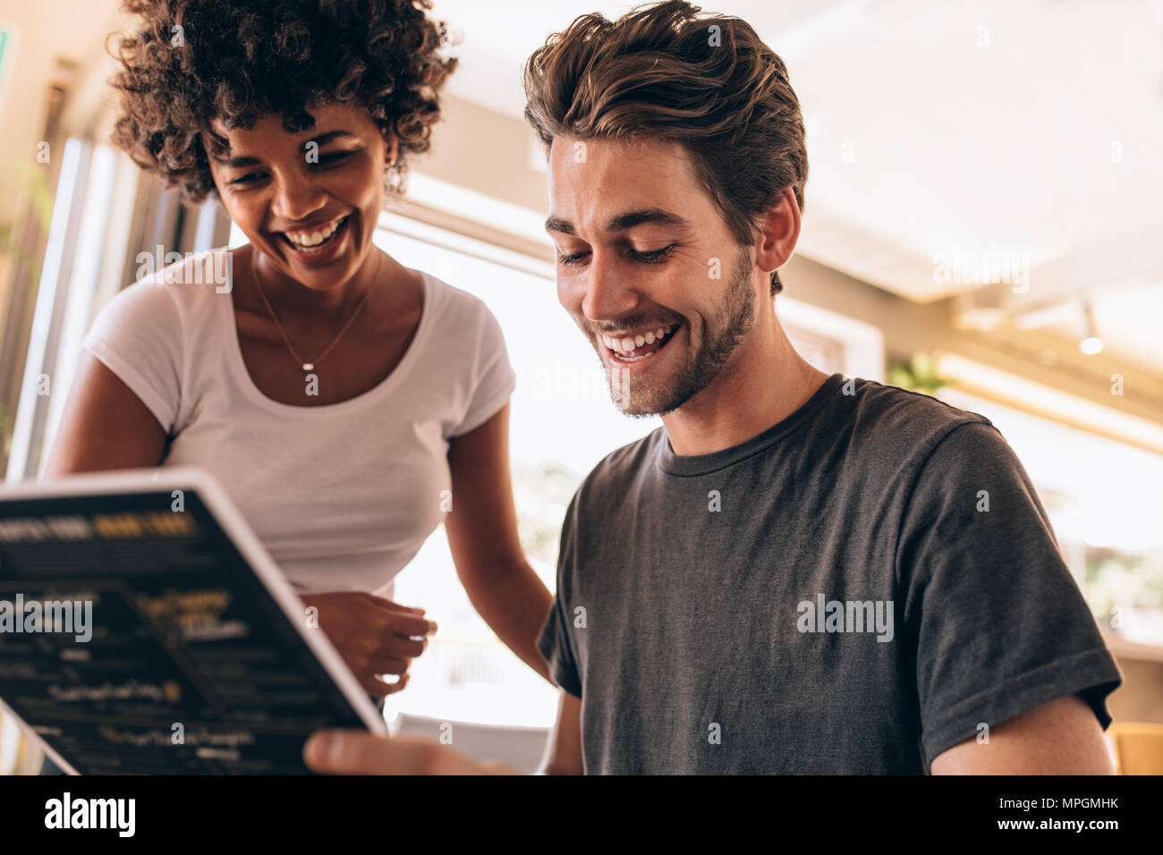 Cheerful young man sitting at cafe holding menu card giving order to a ...