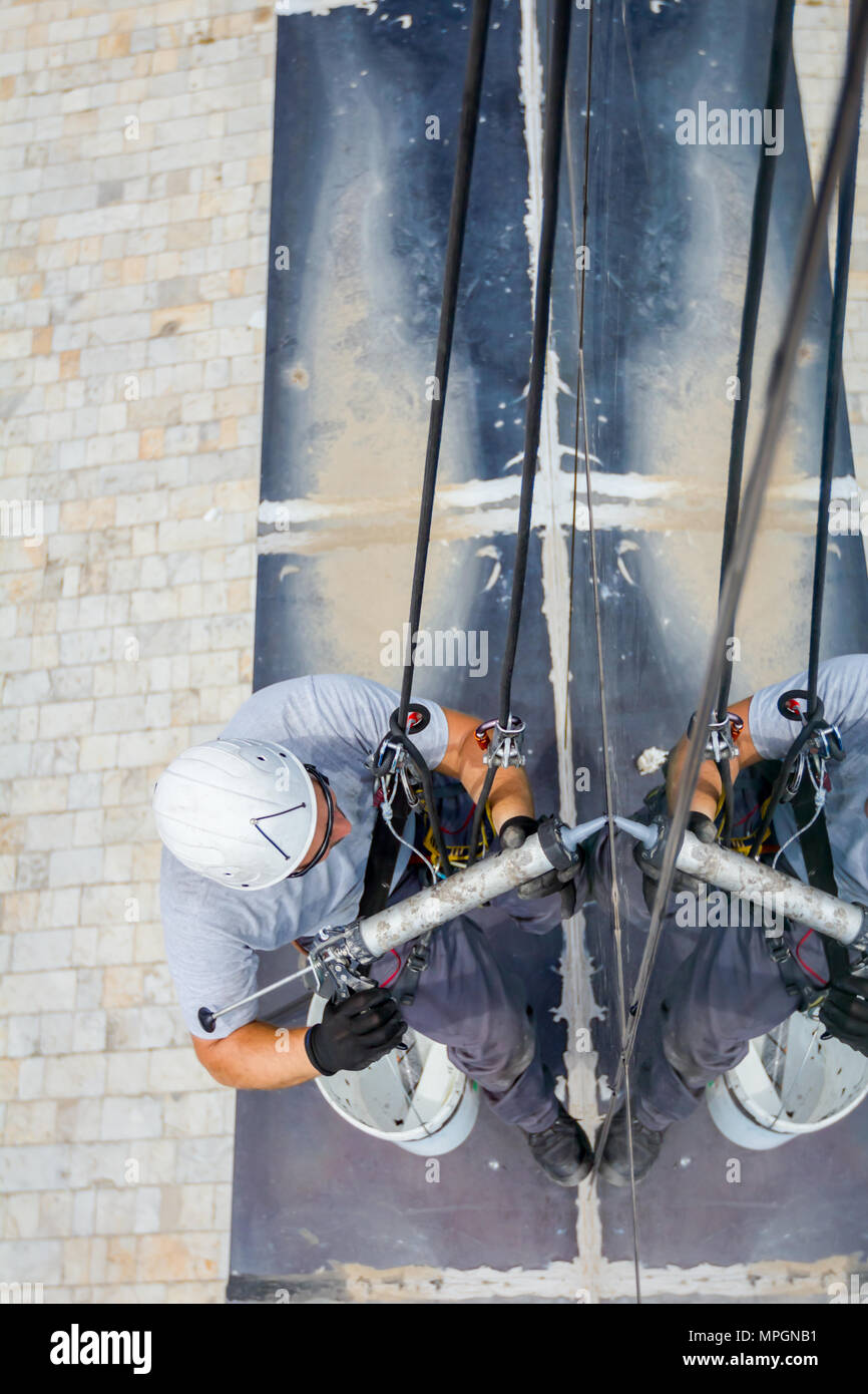 Industrial climber is applying silicone to rubber juncture among ...