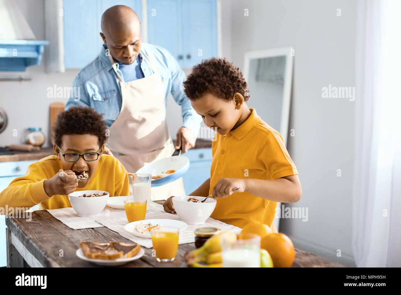 Cute little boys eating breakfast while their father cooking omelet ...