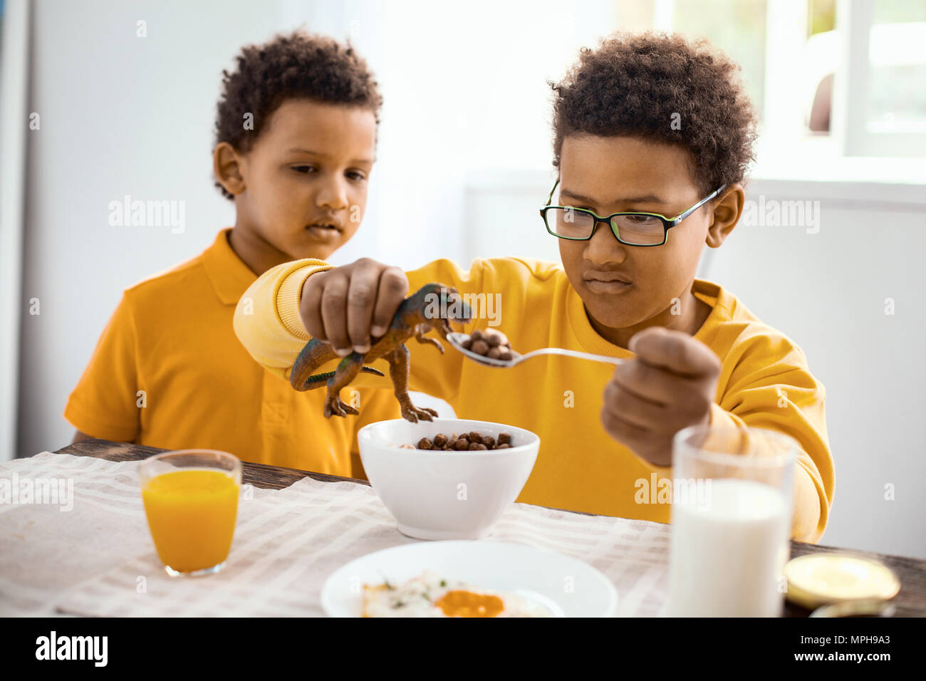 Cute little boy watching his brother feed toy dinosaur Stock Photo - Alamy