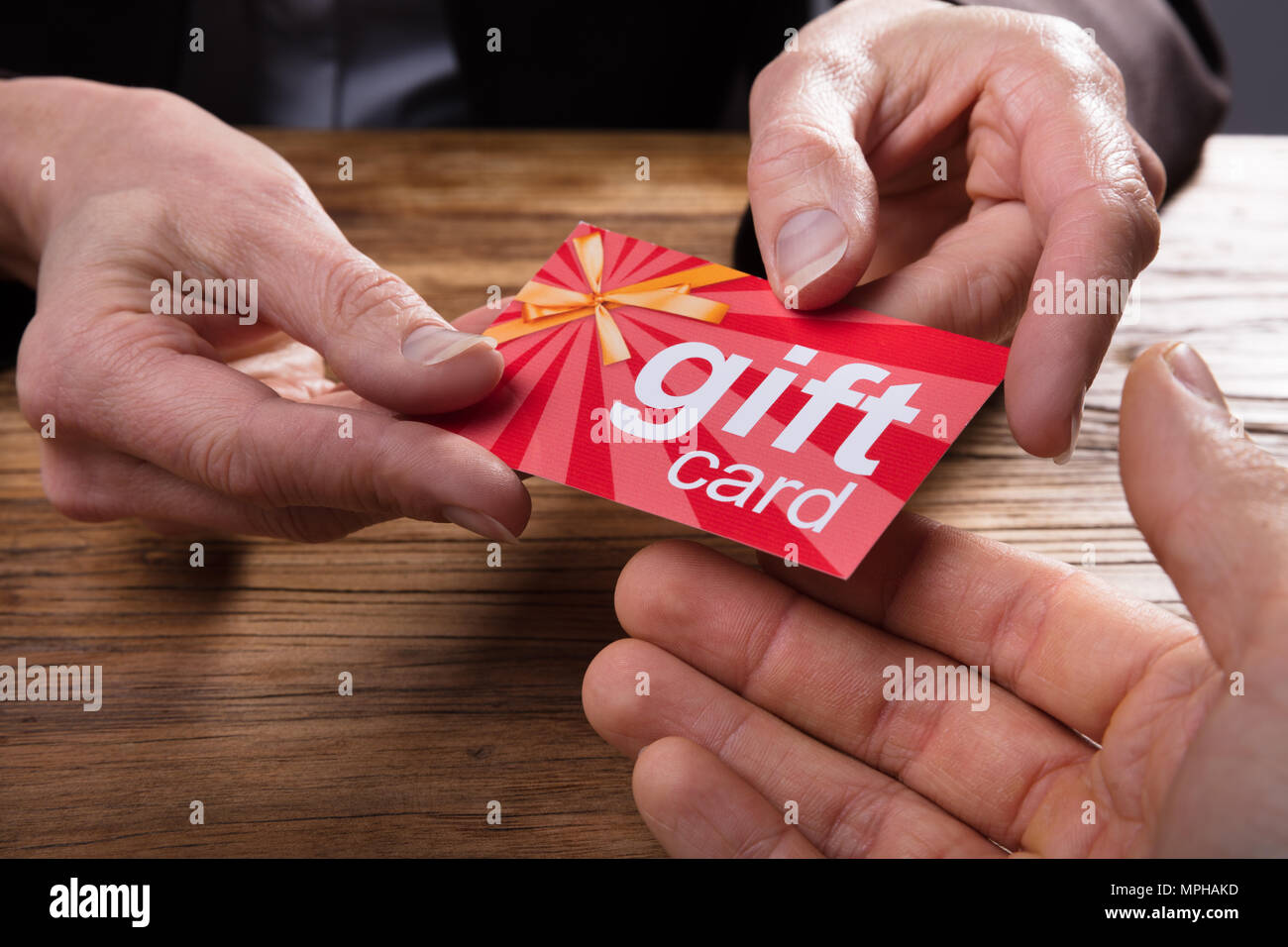 Businessperson's Hand Giving Gift Card To Colleague Over Wooden Desk ...