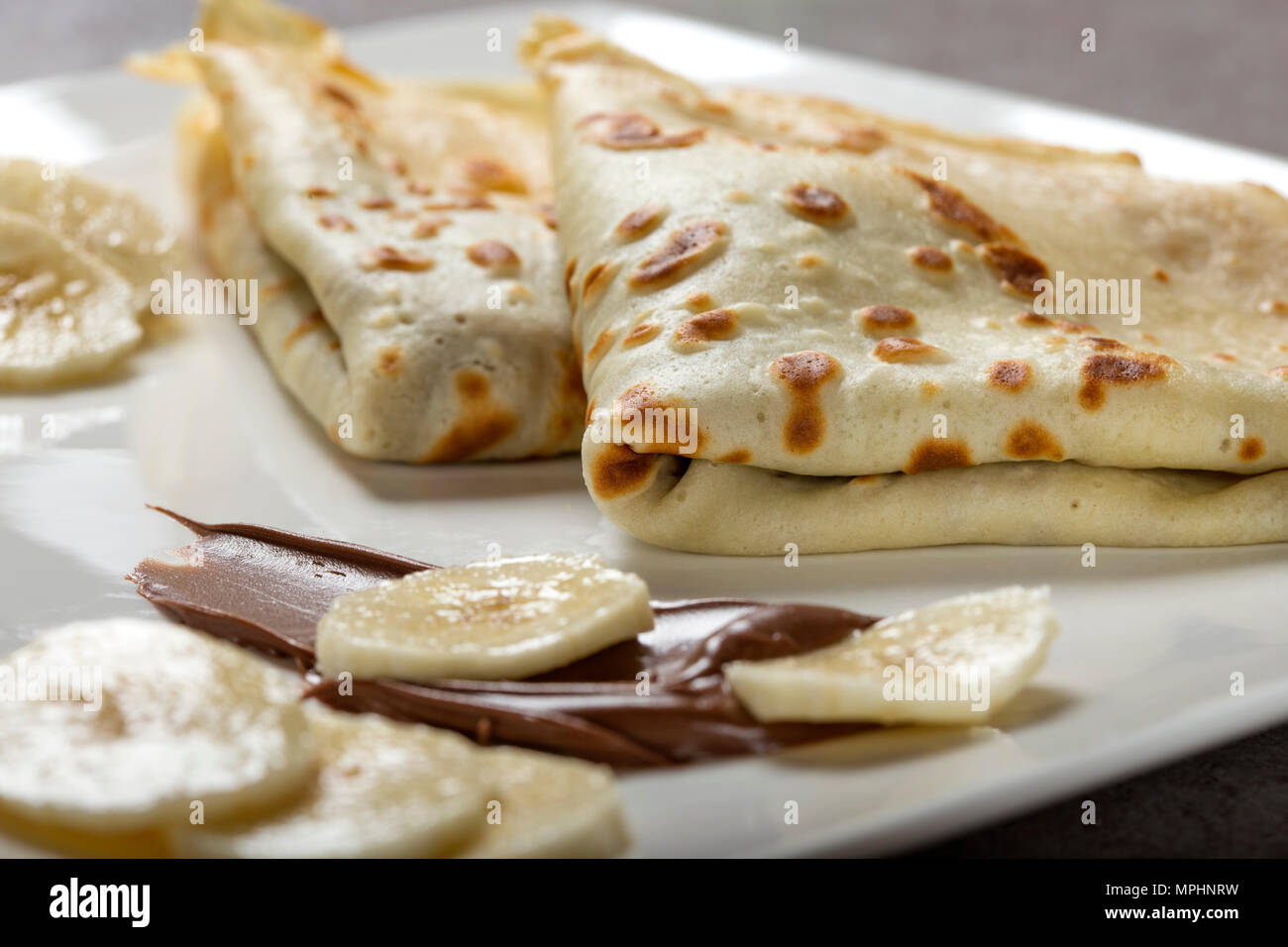 French style crepes with banana, chocolate sauce on a white plate ...