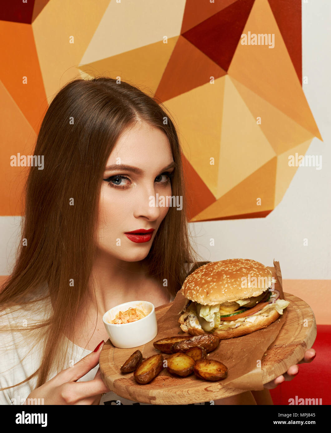 Female model demonstrating burger lying on round wooden plate Stock ...