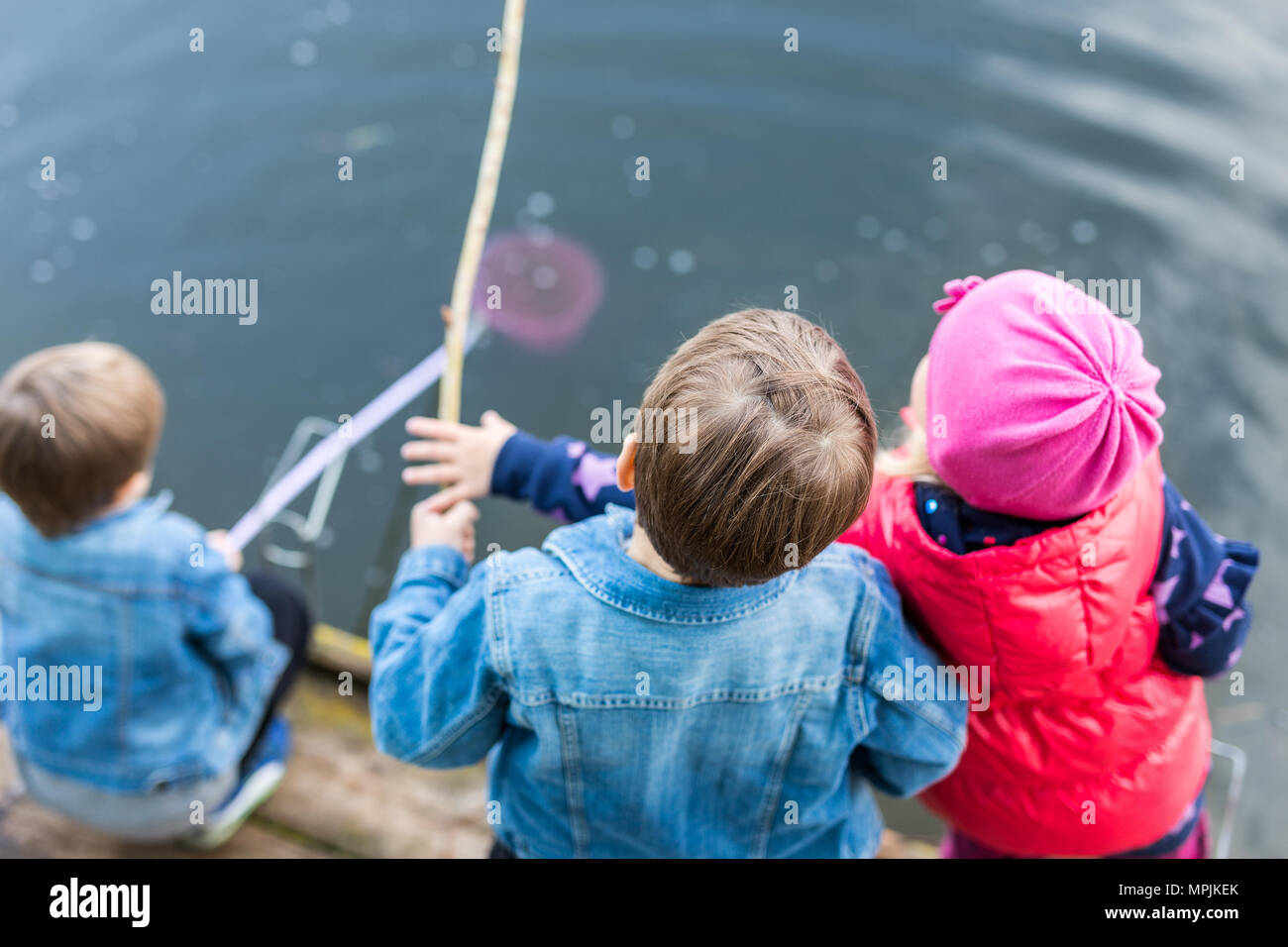 Three friends play fishing on wooden pier near pond. Two toddler boys ...