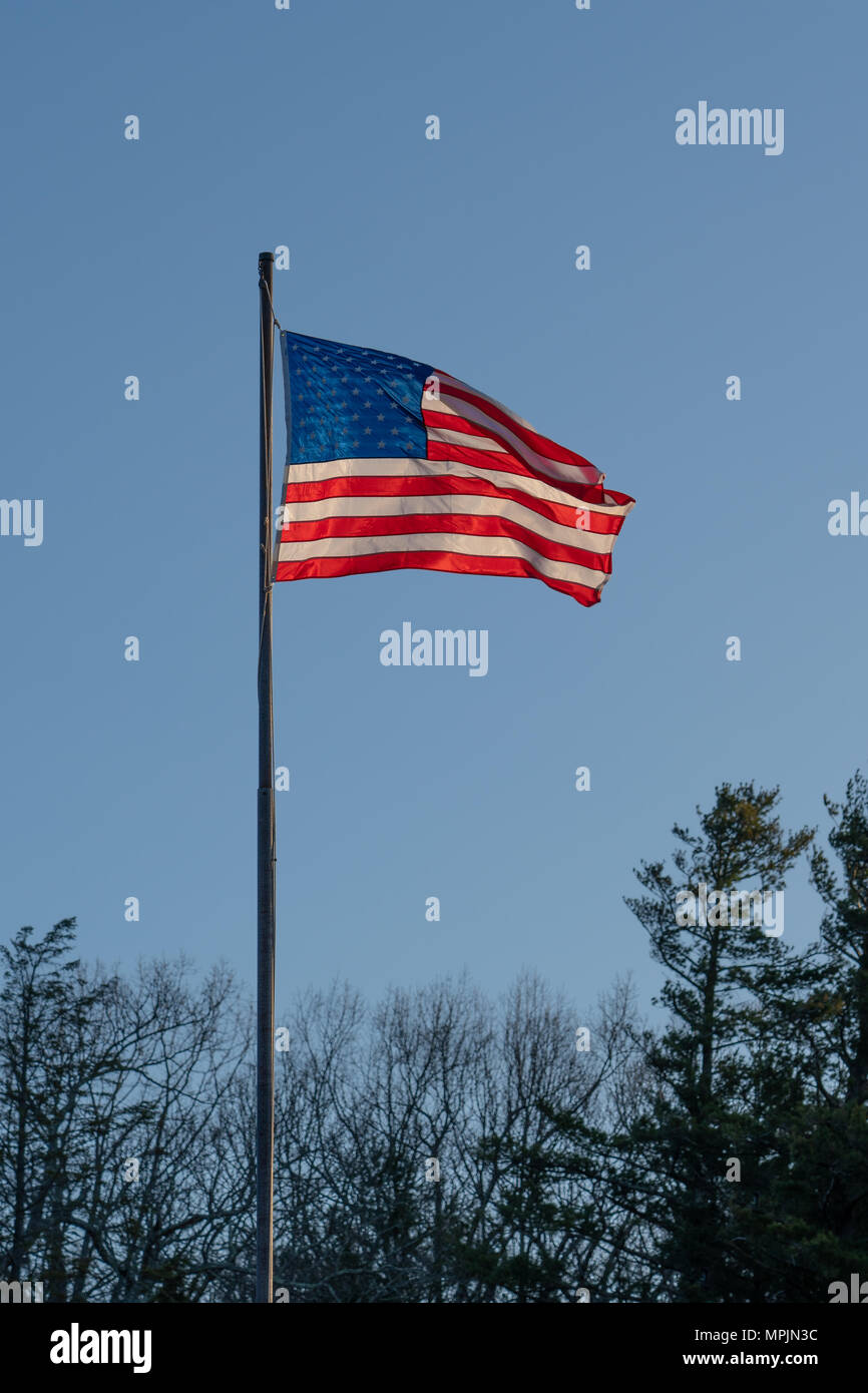 Early morning sun shining through the American flag on a pole with a ...