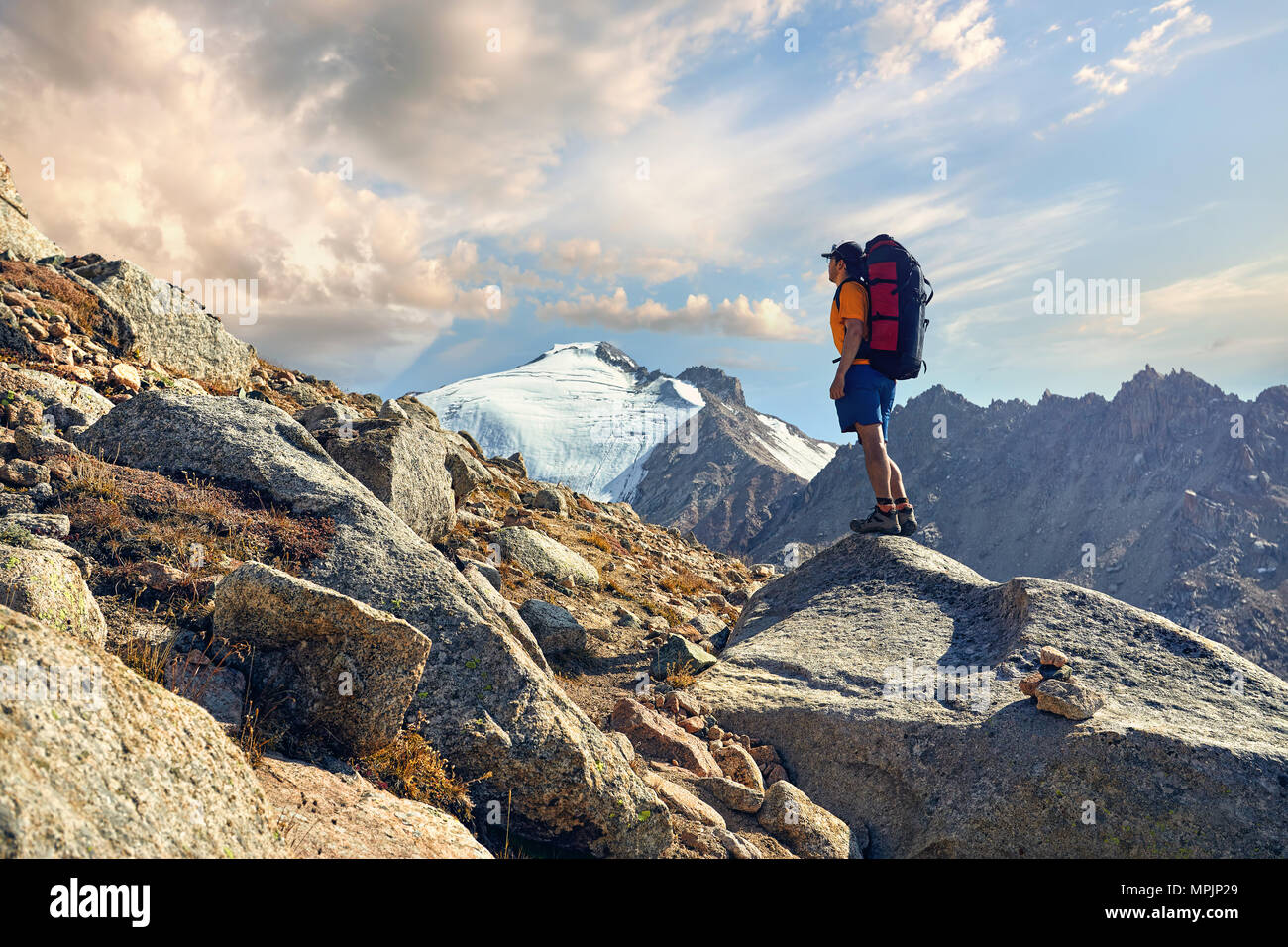 Hiker in orange shirt with big backpack looking on the snowy summit at ...