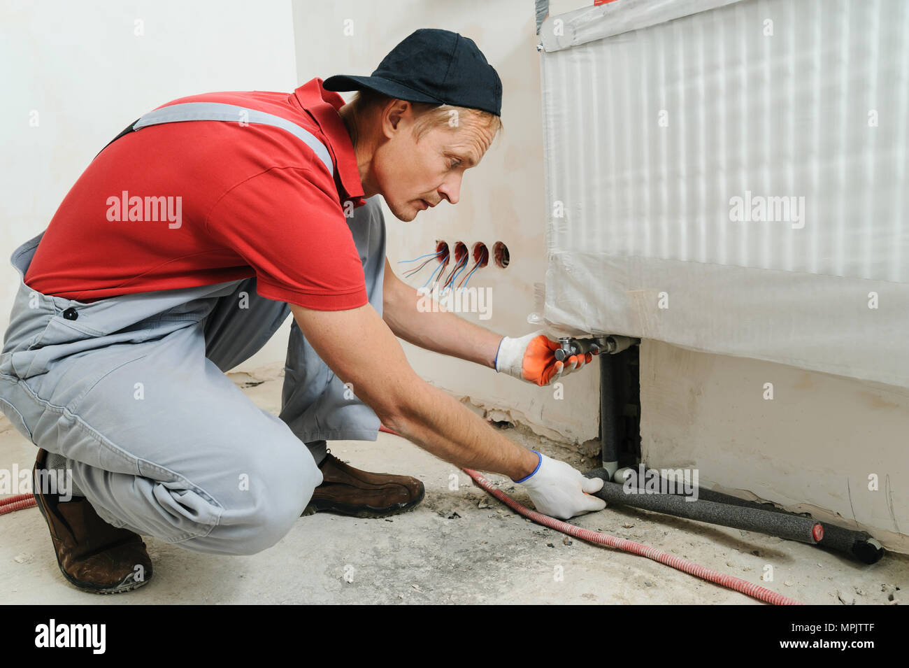 Installation of home heating. Worker attaches the pipe to the radiator ...