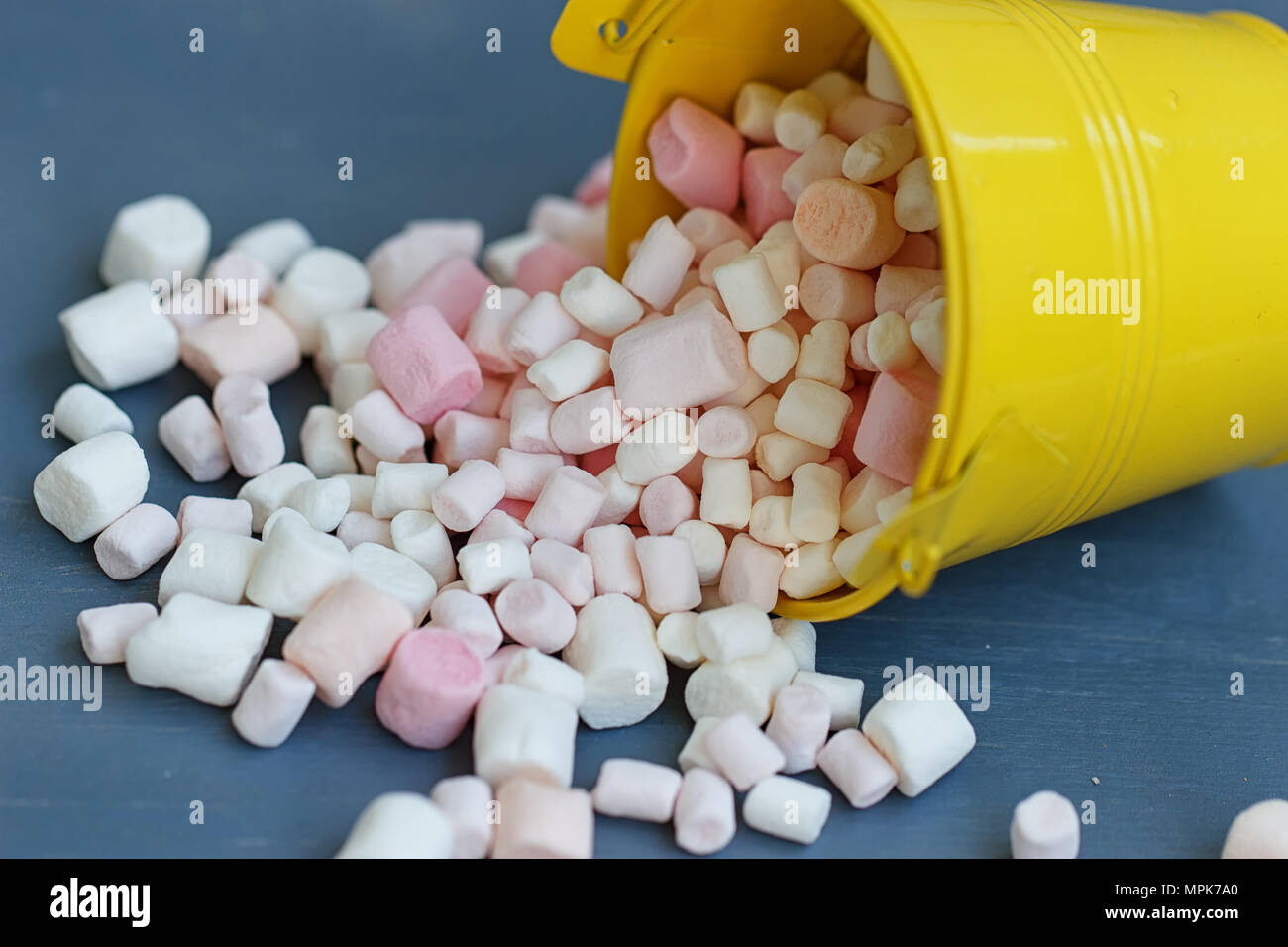 Yellow bucket full of marshmallow scattered on the blue Board Stock ...