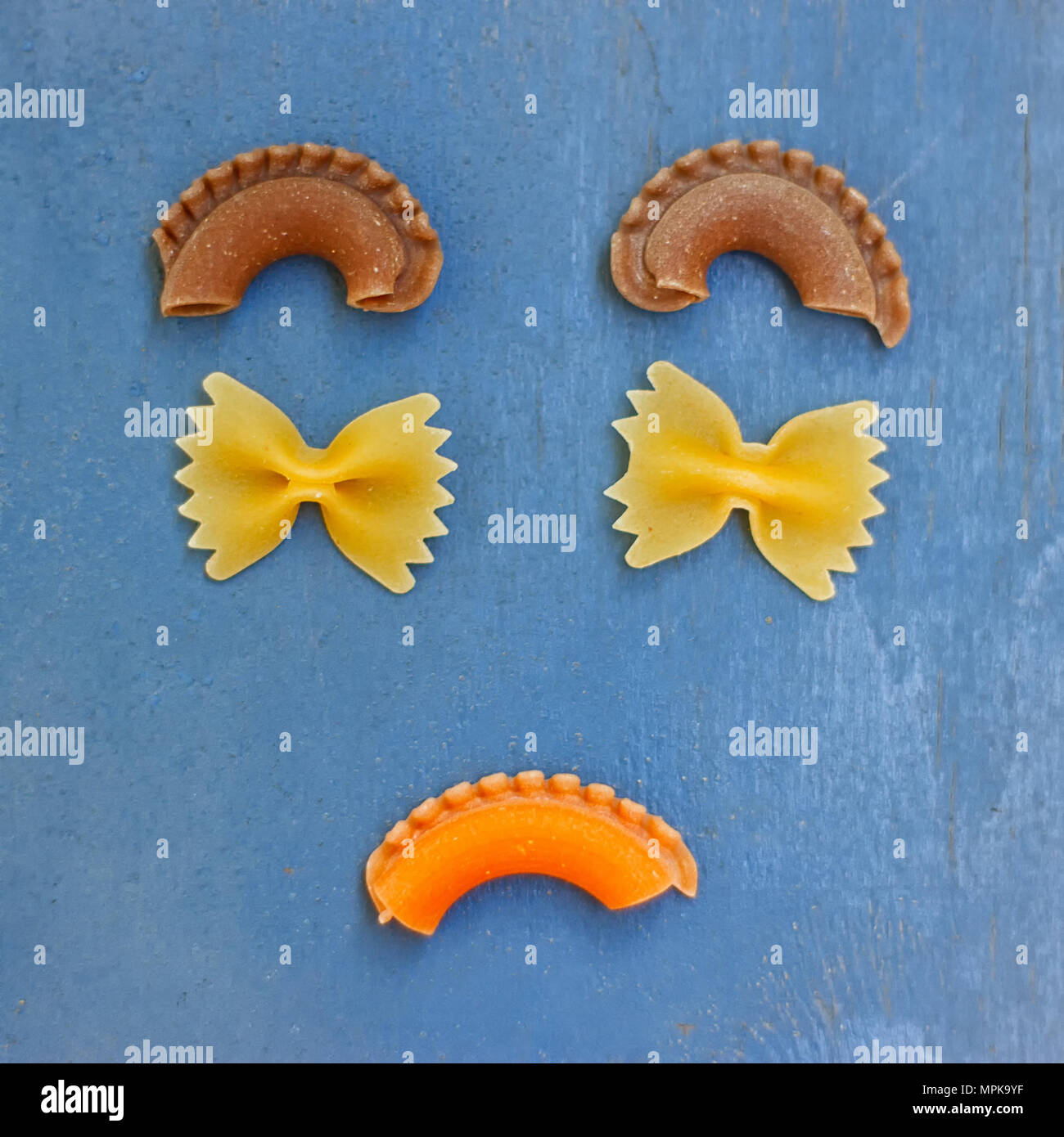 sad face with raw pasta on blue background Stock Photo - Alamy