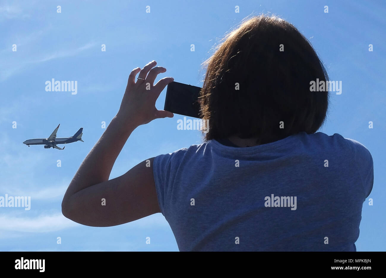 A girl is photographing a plane flying in the sky Stock Photo - Alamy
