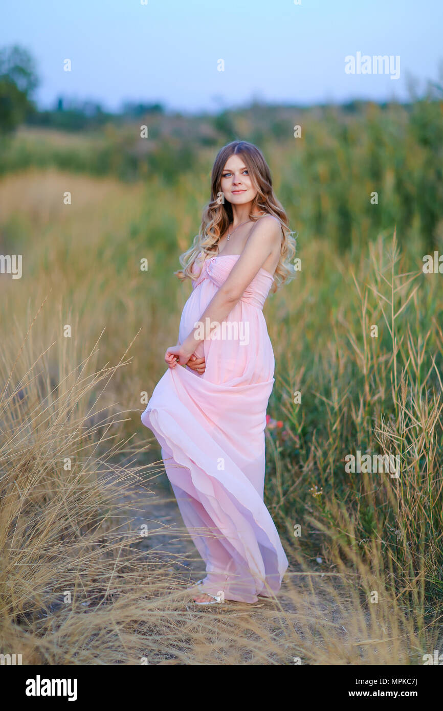 Pregnant female person wearing pink dress standing in steppe background ...