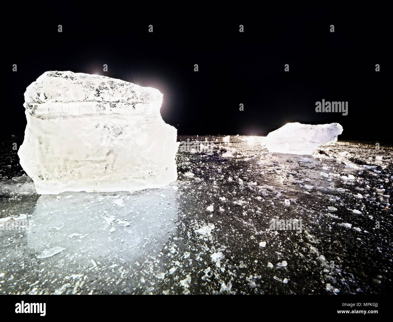 Blue ice cubes shine on flat glacier surface. Thanks to spot light ...