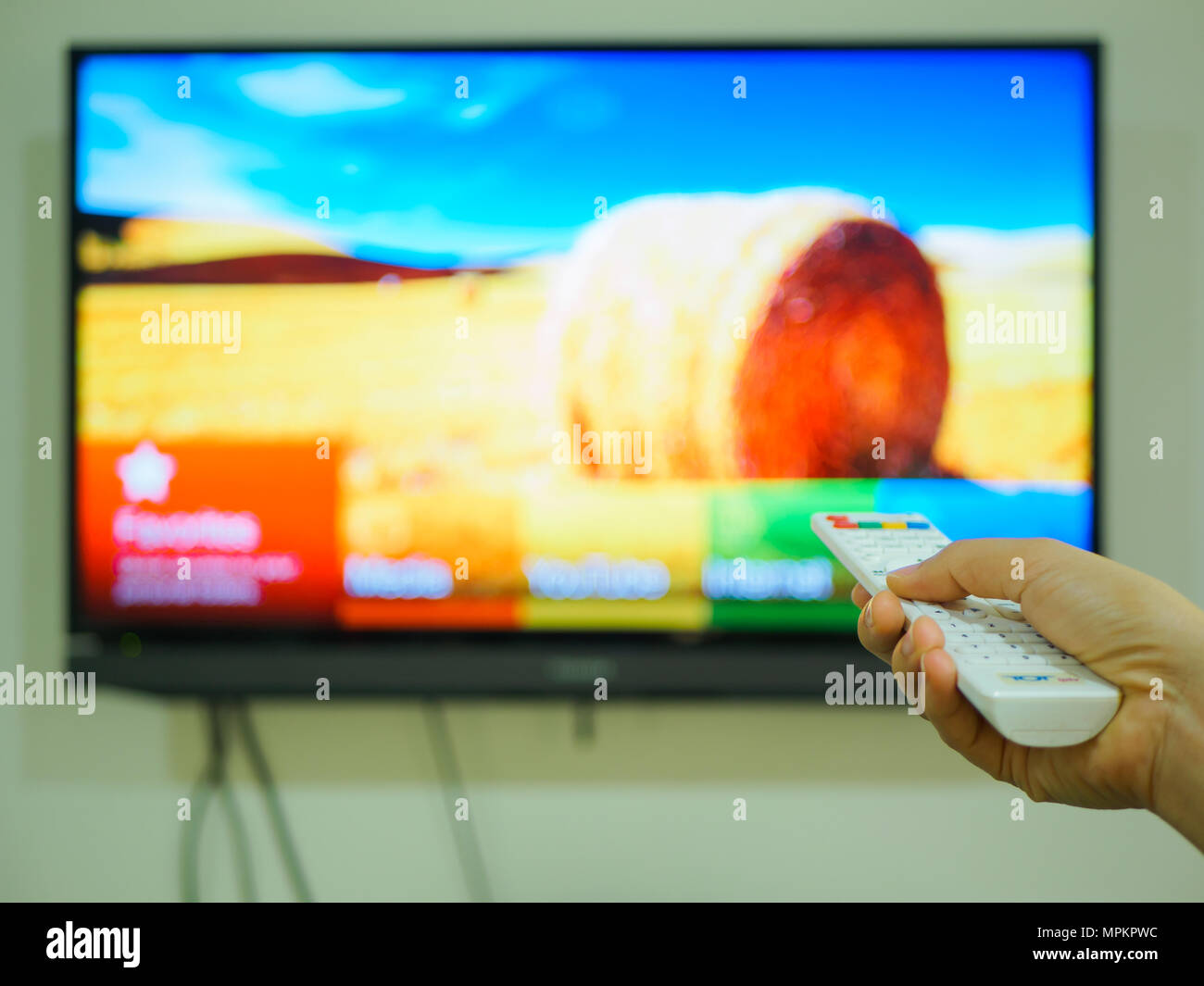 Close up Hand holding TV remote control with a television in the ...