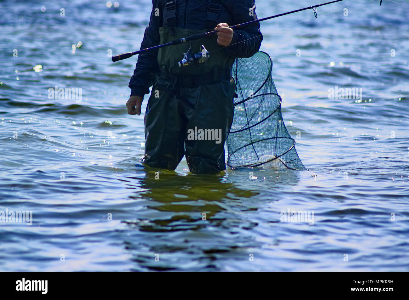 A man with a fishing net and a fishing rod is going on beach in water ...