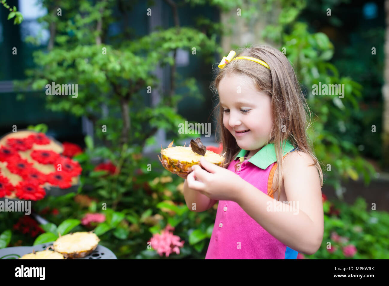Child watching butterfly at tropical garden. Little girl feeding exotic ...