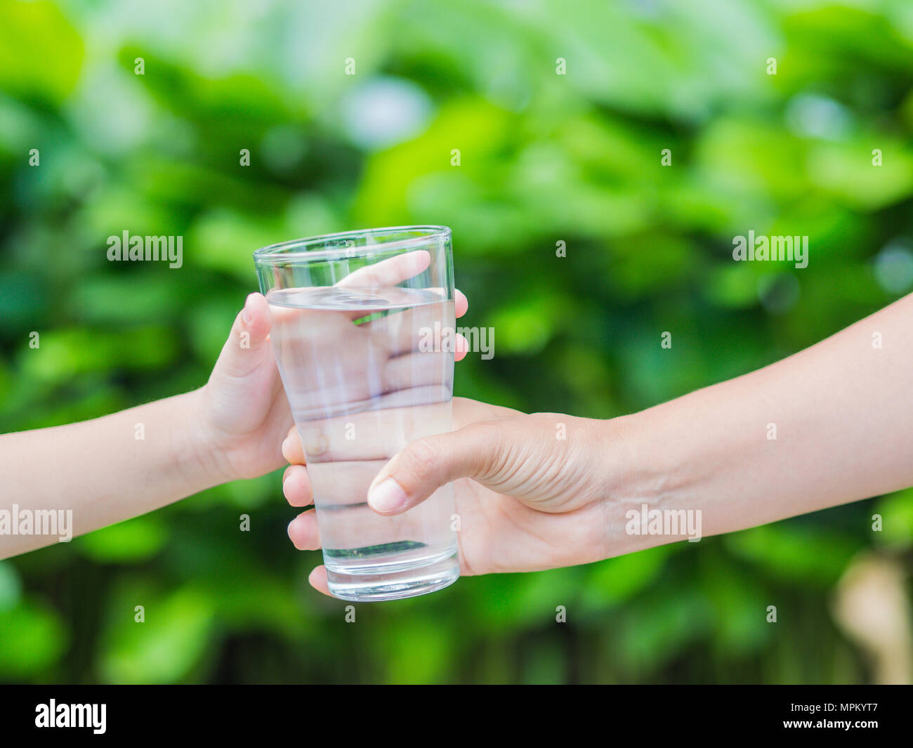 Woman hand giving glass of fresh water to child on the green grass ...