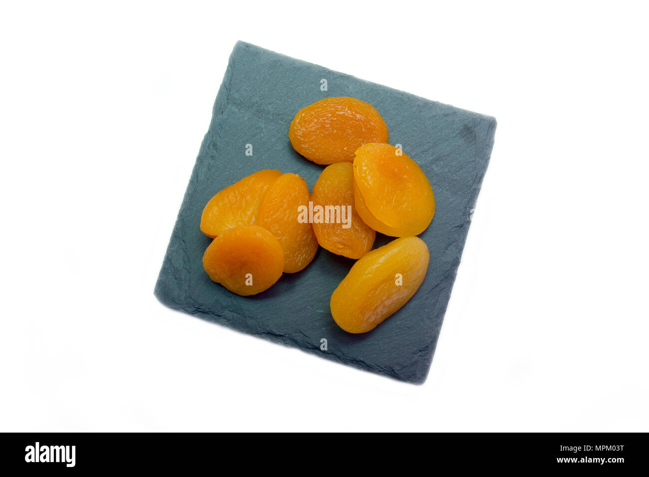Pitted apricots on slate tray on a white background viewed from above ...