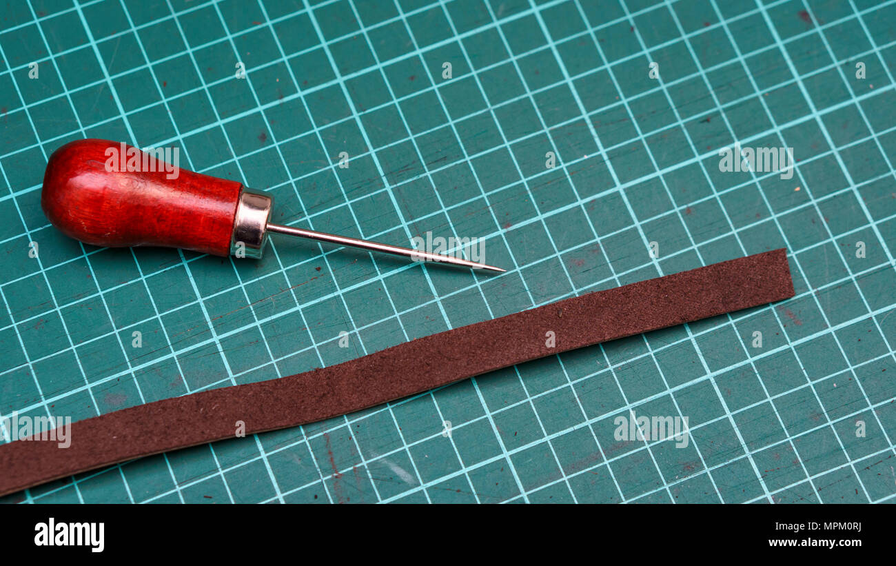 Tool of a tanner close-up. Awl and piece of leather lies on rug for ...