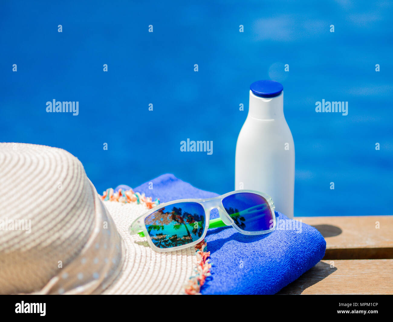 Beach hat, sunglasses, blue towel and sunscreen at the side of swimming ...