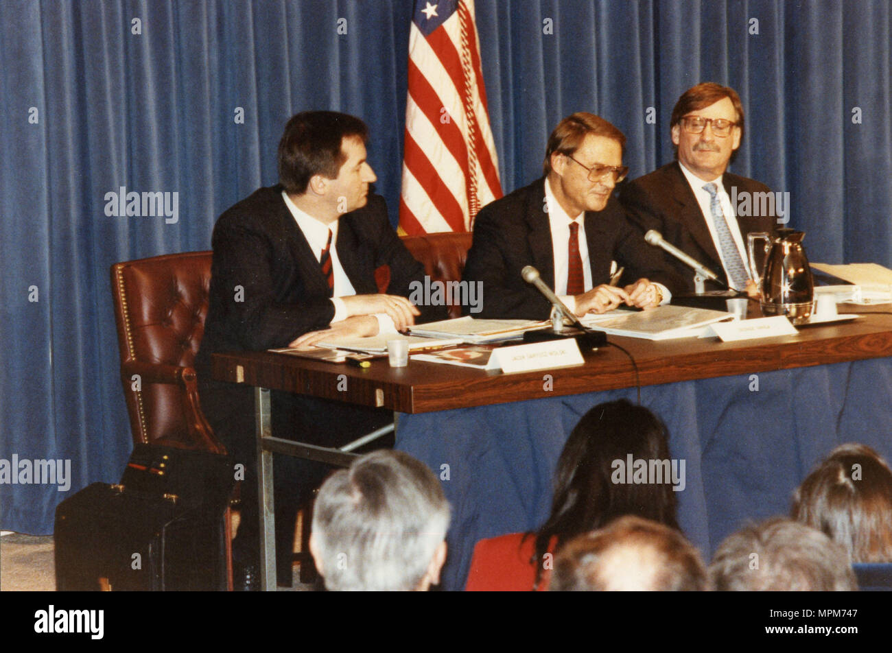 THREE MEN AT THE TABLE ARE HAVING A CONVERSATION WITH A GROUP OF PEOPLE ...