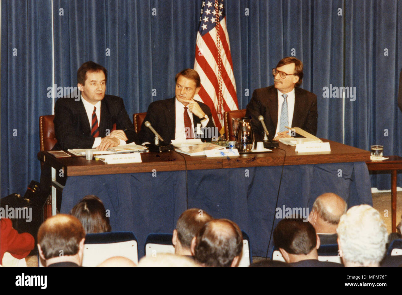 THREE MEN ARE SITTING AT THE TABLE HAVING A CONVERSATION WITH A GROUP ...