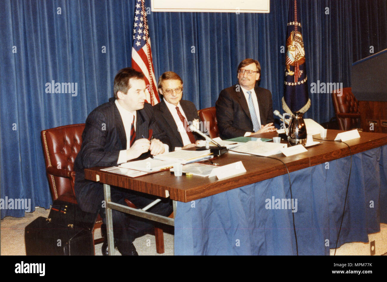 THREE MEN ARE SITTING AT THE TABLE HAVING A CONVERSATION WITH A GROUP ...